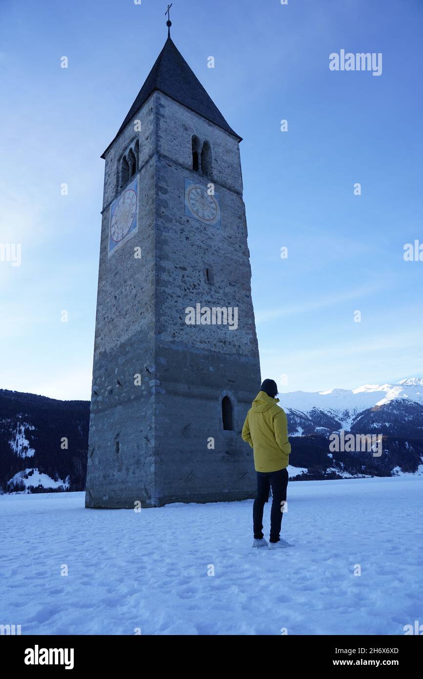 Man stands on a frozen lake at the Reschen Pass in winter. Südtirol ...