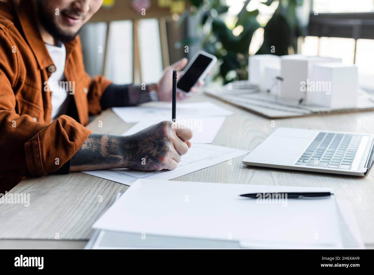 cropped view of blurred architect with mobile phone drawing blueprint ...