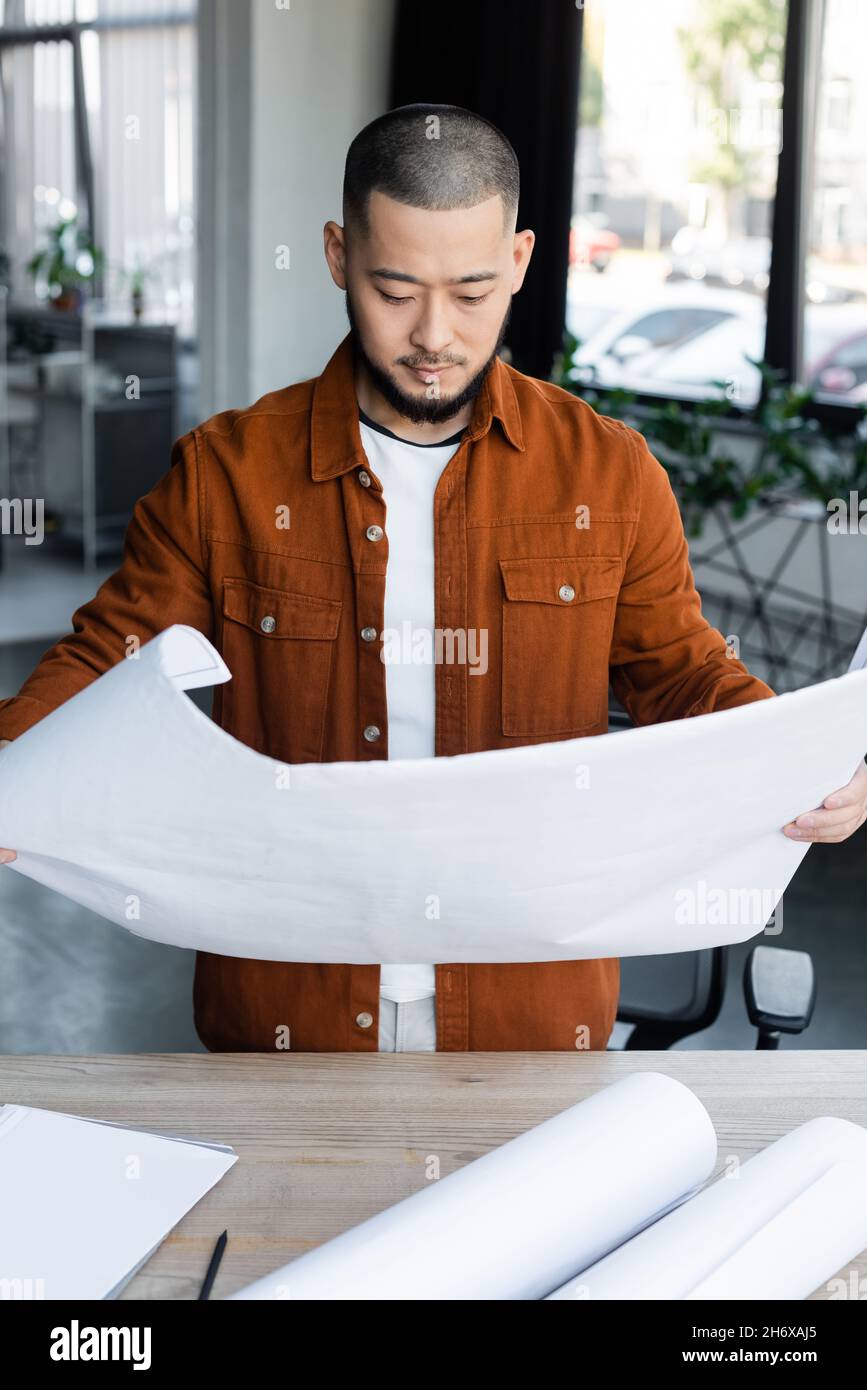 asian engineer looking at blueprint while working in architectural ...