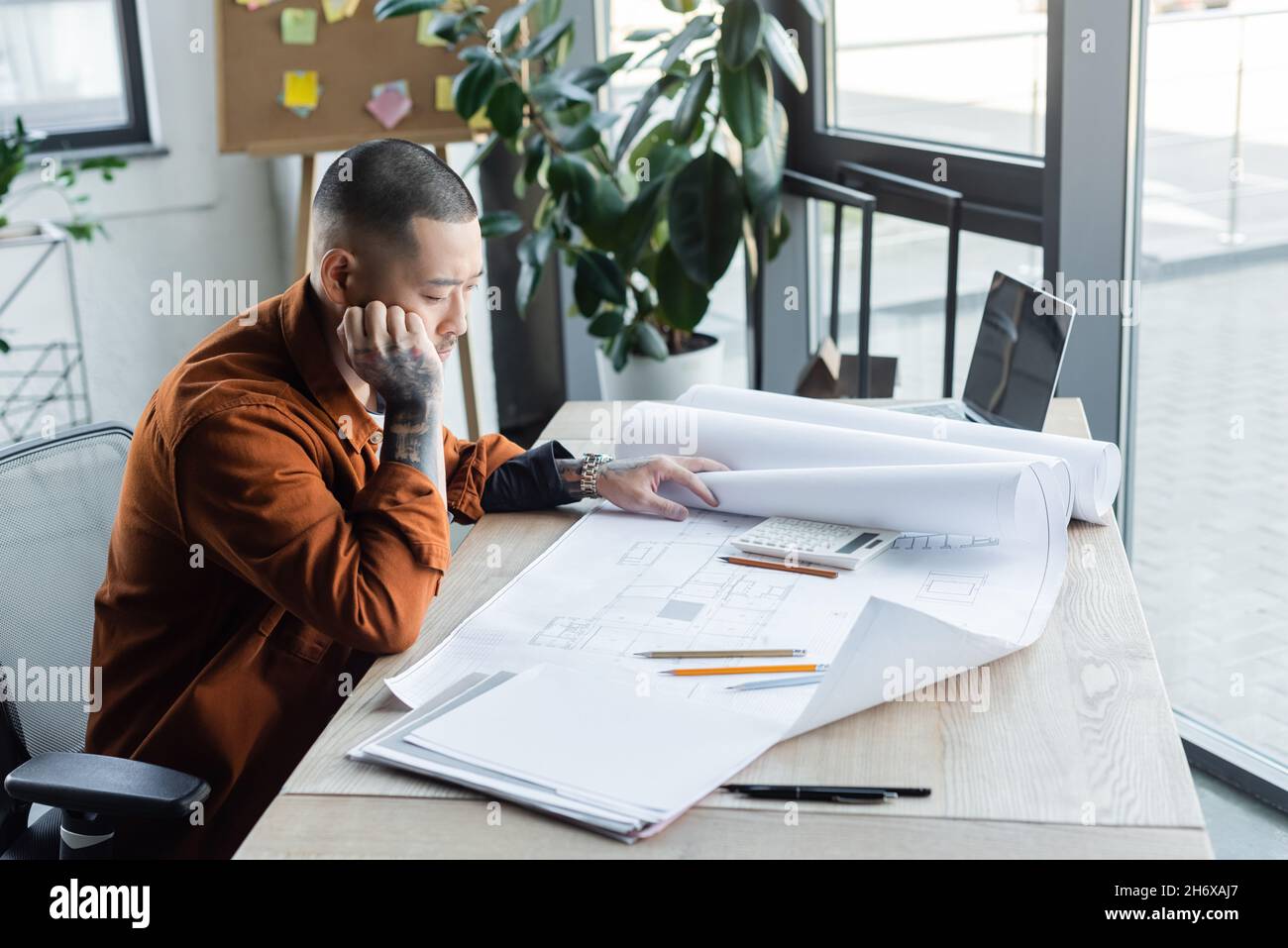 thoughtful asian architect looking at blueprint while working in ...