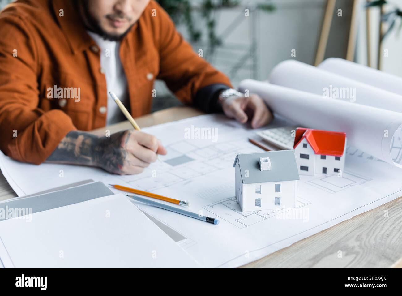 cropped view of blurred architect drawing blueprint near house models ...