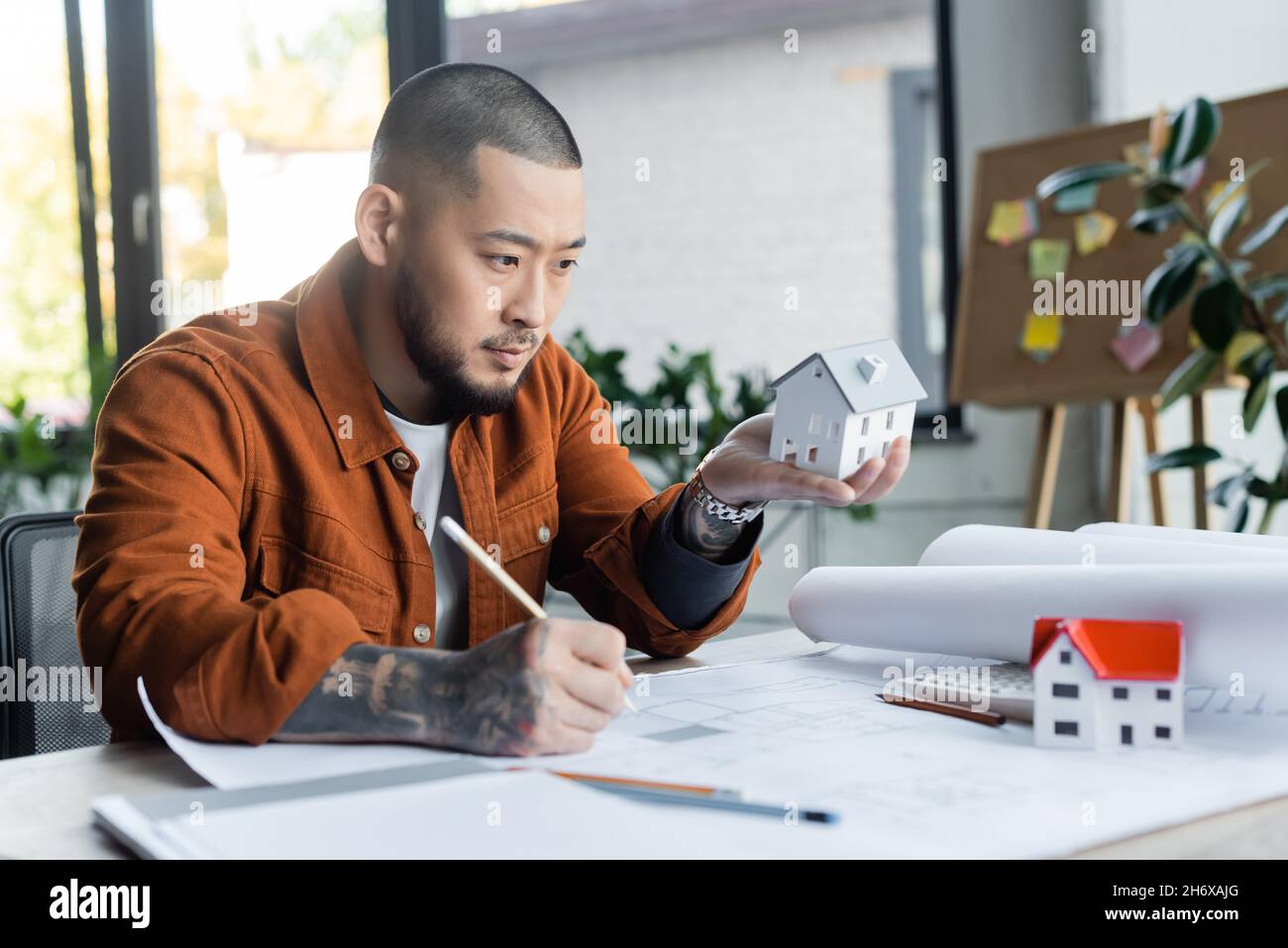 asian architect holding house model while drawing blueprint in office ...