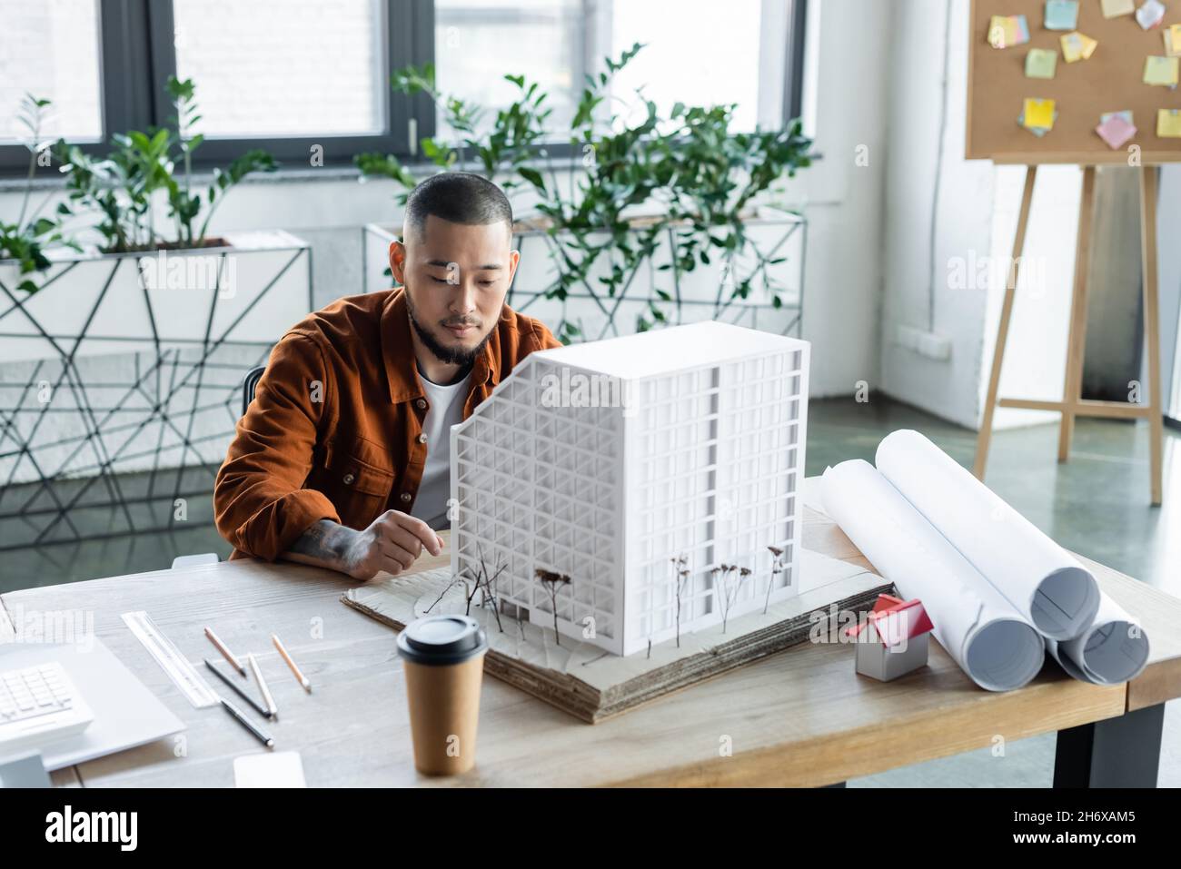 asian architect sitting near house model while working on architectural ...
