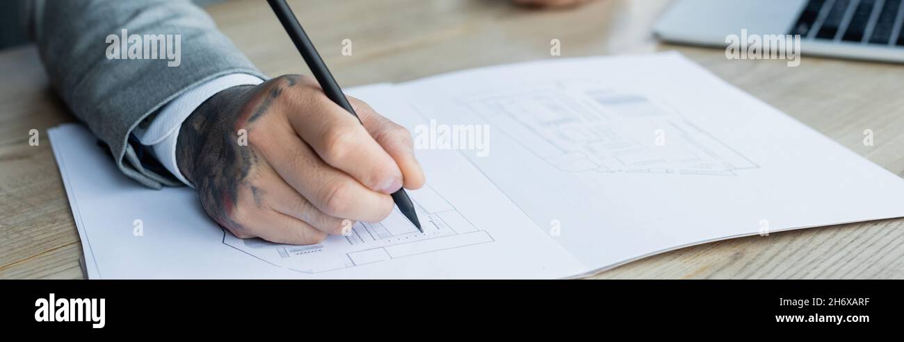 partial view of tattooed architect drawing blueprint at workplace ...
