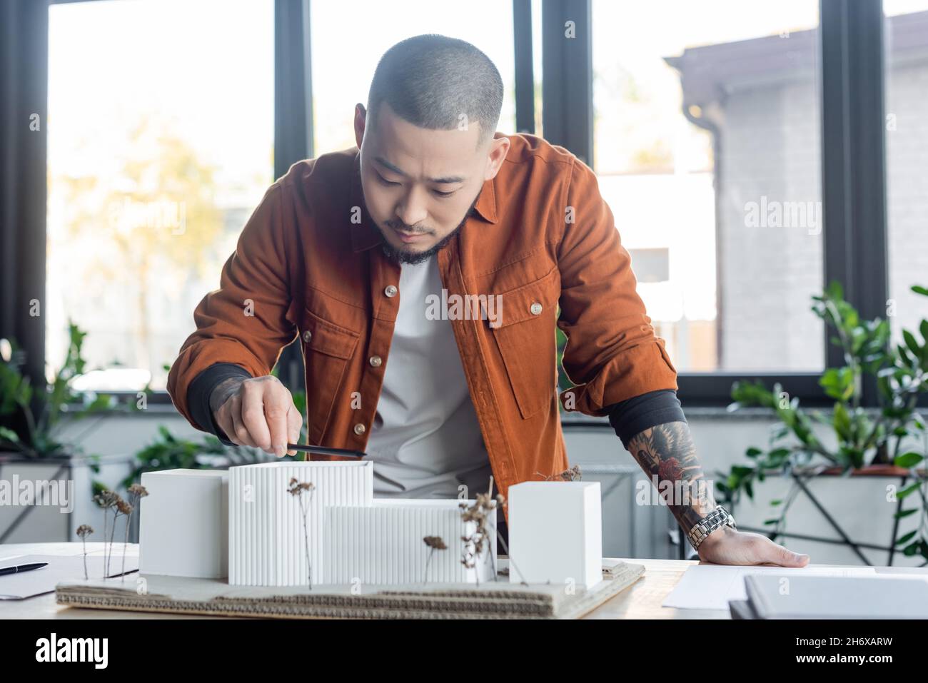 tattooed asian architect measuring house models with pencil while ...