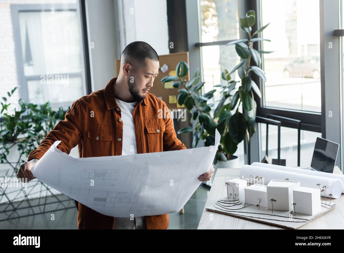 asian architect looking at house models on desk while holding blueprint ...