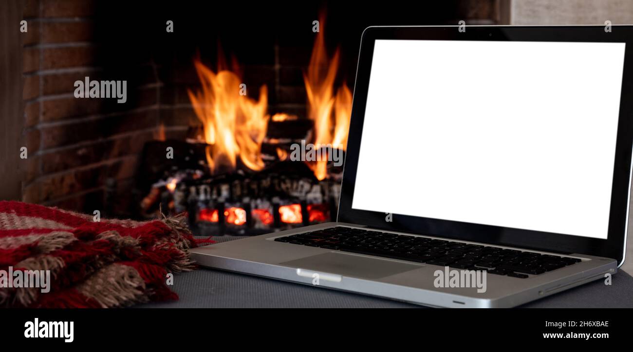 Winter home office concept. Blank screen laptop on burning fireplace ...