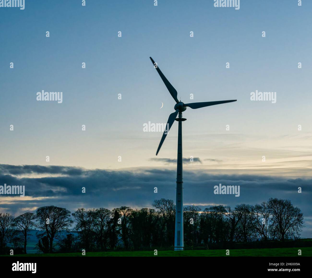 A crescent moon rises the blades of a wind turbine, East Lothian ...