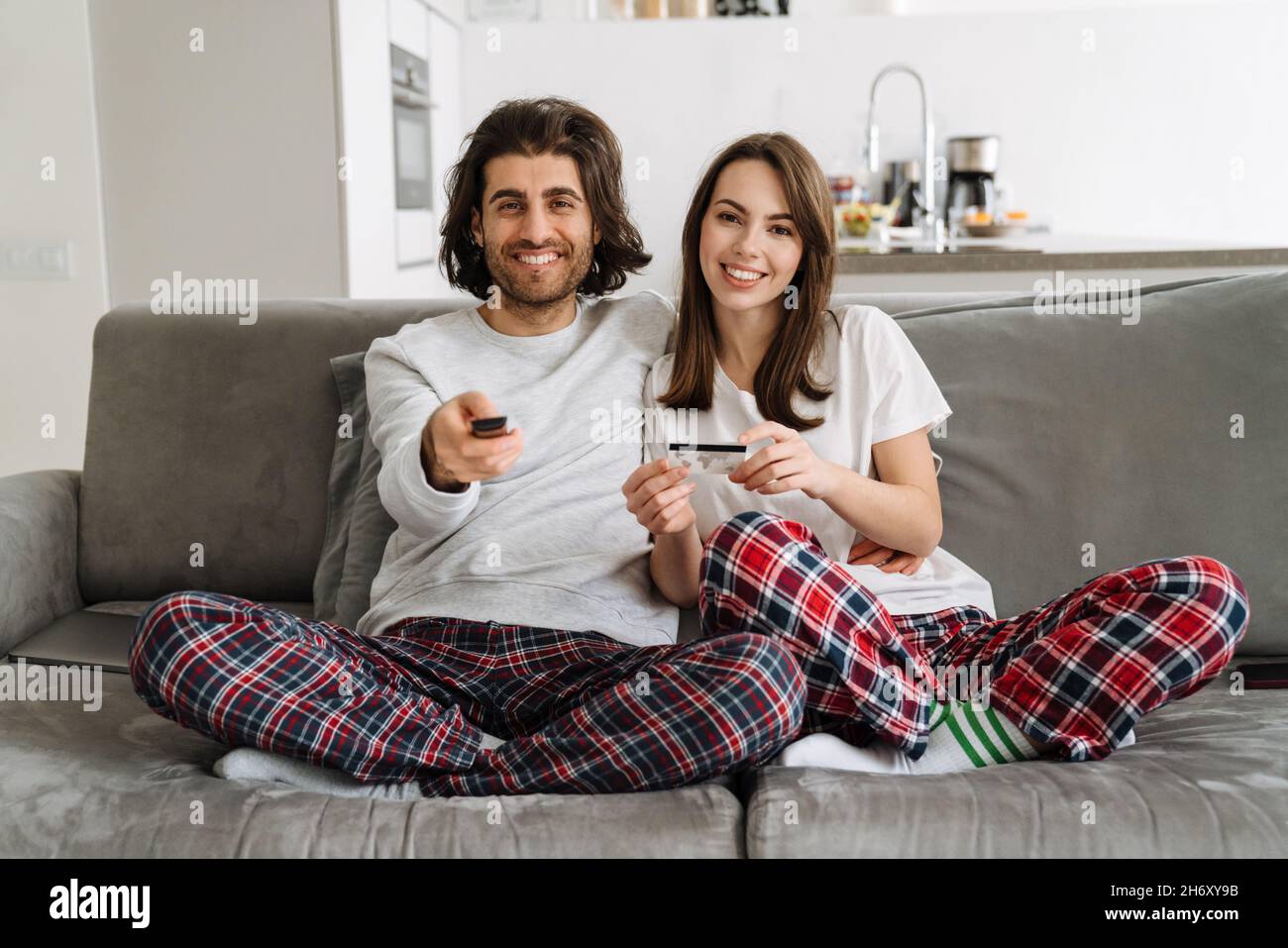 Young multiracial couple using credit card while watching tv together ...