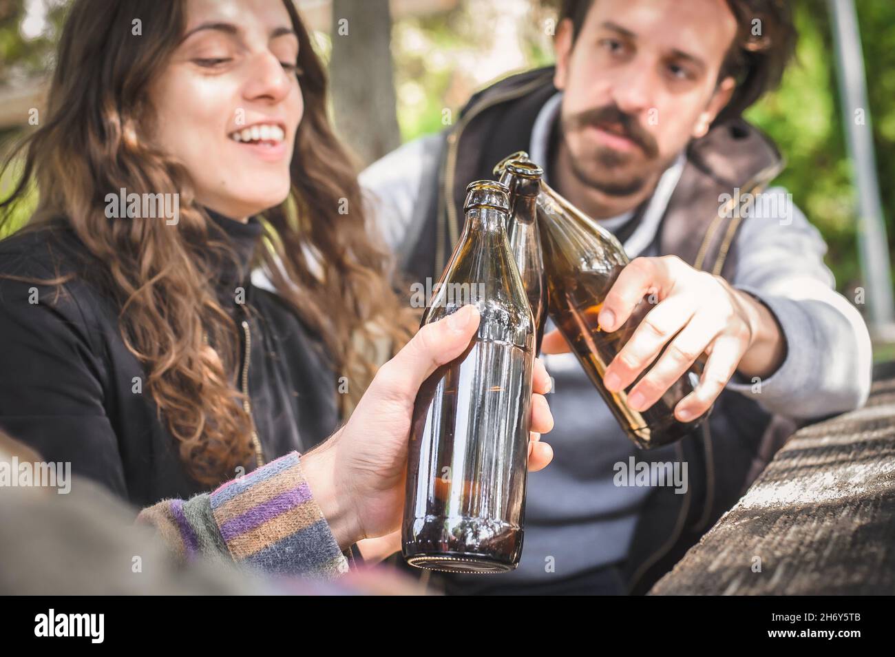 Cheers. Smiling cheerful young friends drinks beer from bottle on ...