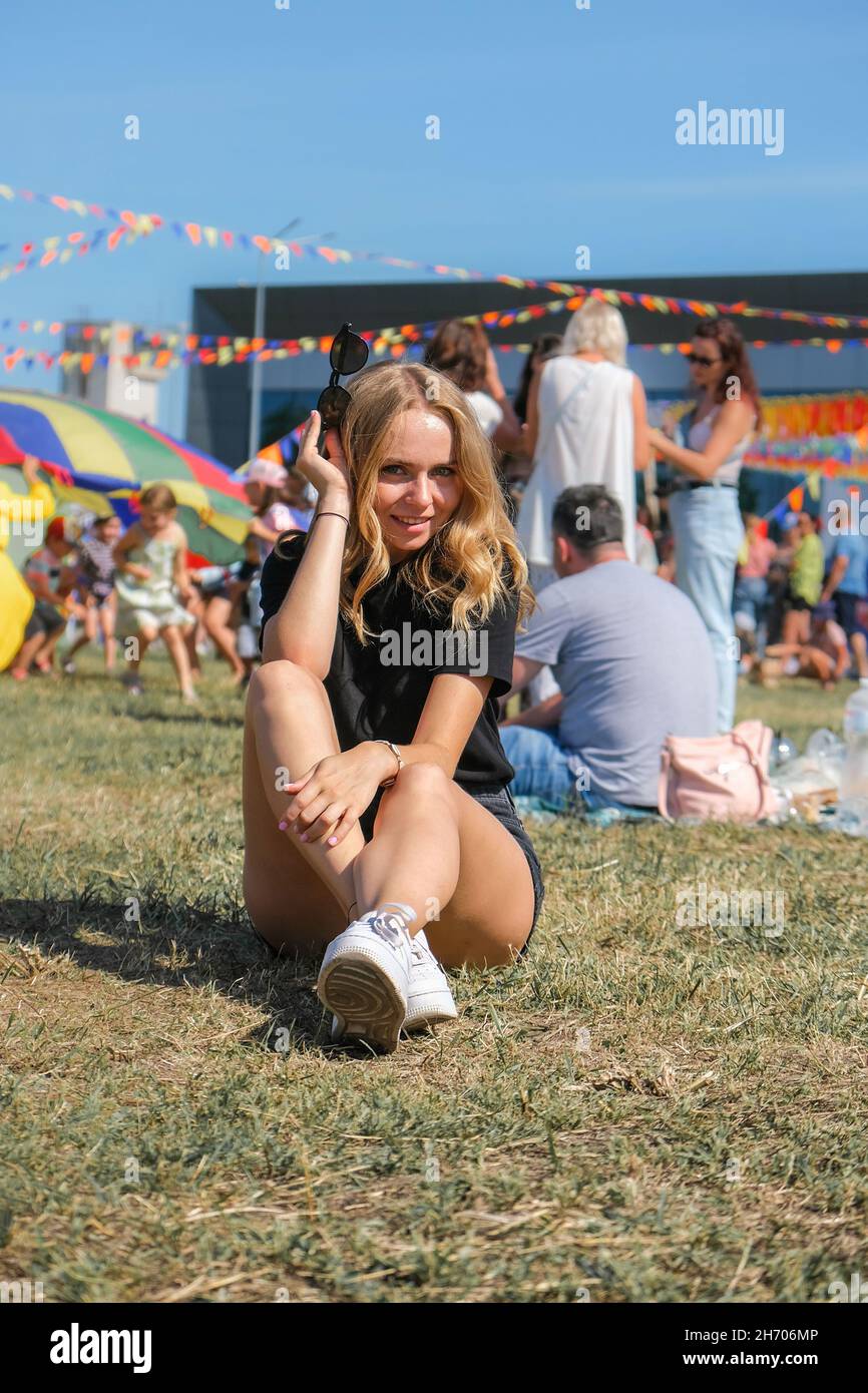 Young woman sitting on grass on festival. Gen z girl enjoying outdoors ...