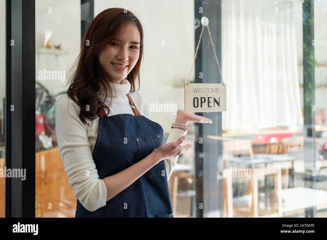 Portrait of a smiling Asian entrepreneur standing behind her cafe ...