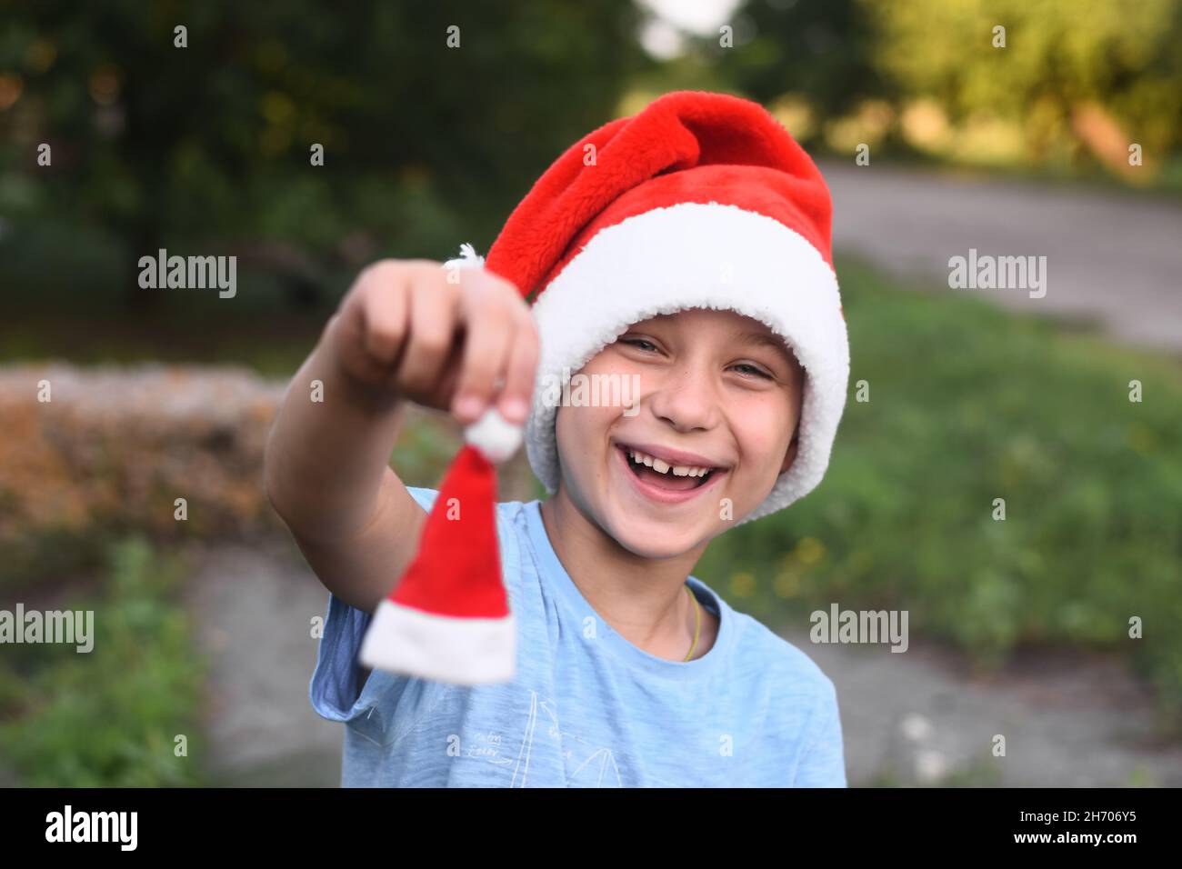 a laughing boy in a Santa hat holds a small Santa helper hat in his ...