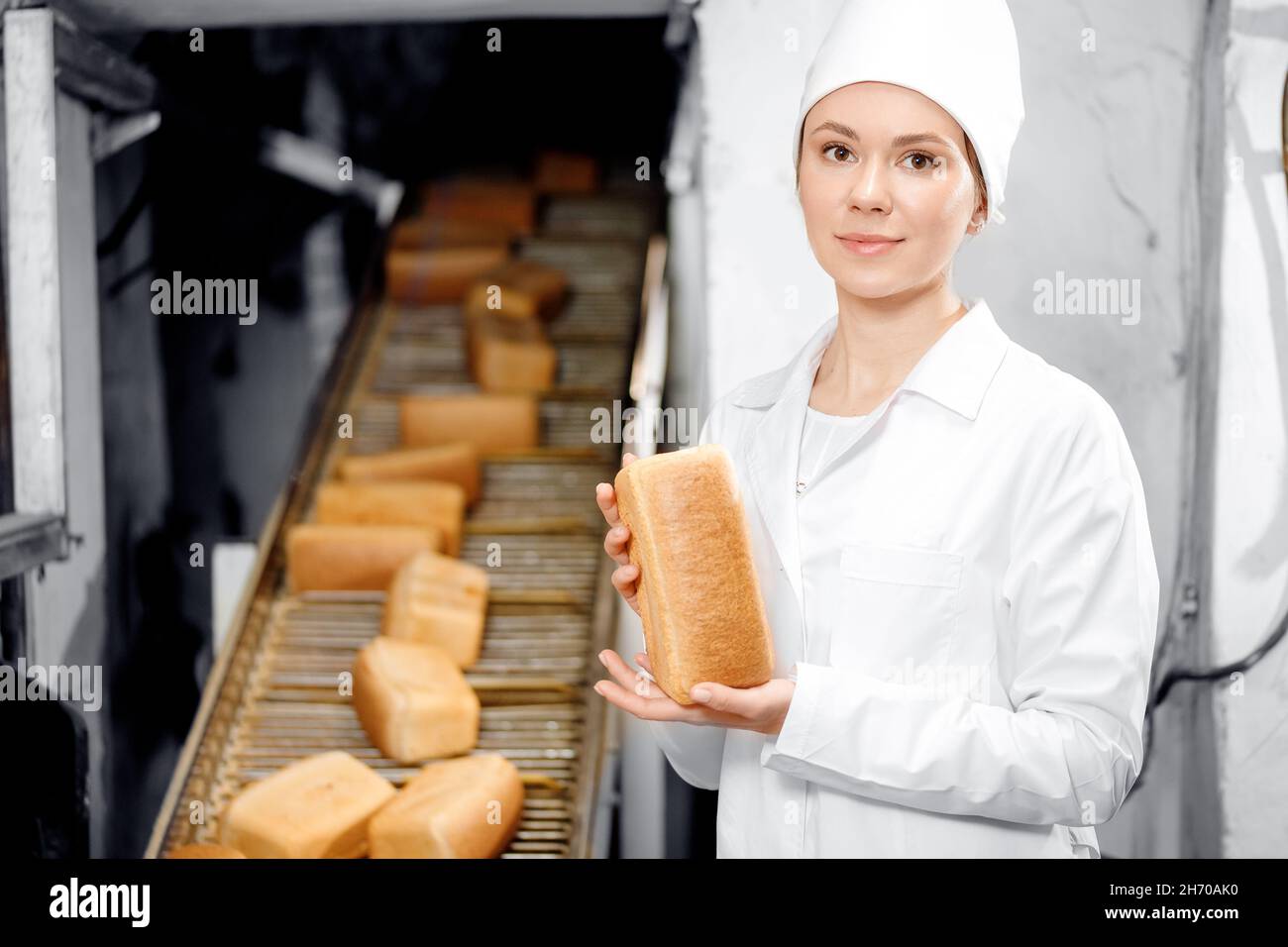 Baker woman holding fresh bread in hands on background automatic ...