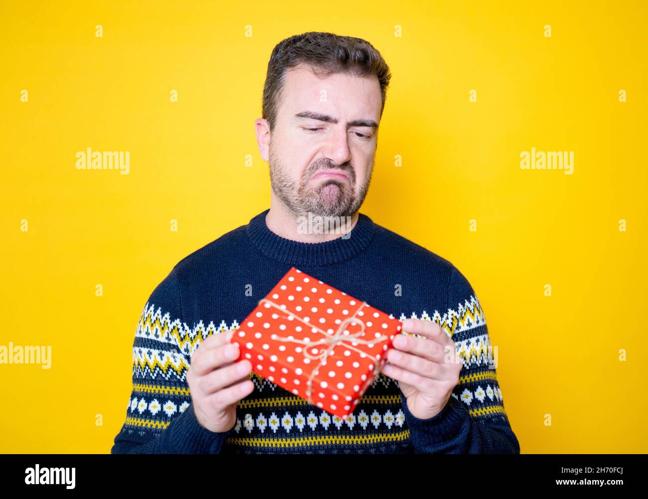 Portrait of one disgusted man holding red box gift on yellow background ...