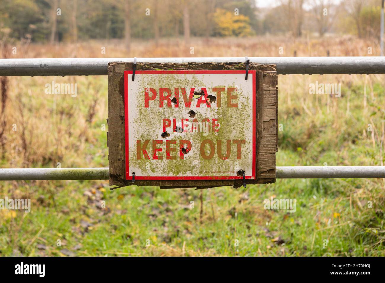 A dirty Private Please Keep Out sign with bullet holes on a metal gate ...