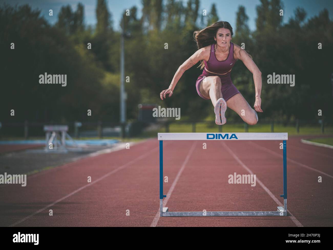 Athlete model girl jumping hurdles on the running track Stock Photo - Alamy
