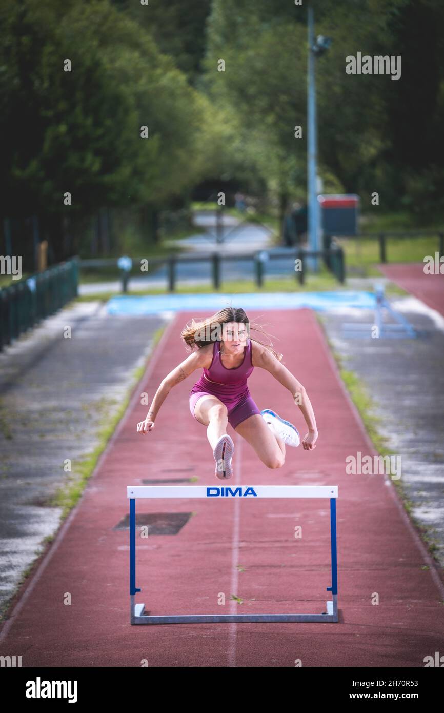 Athlete model girl jumping hurdles on the running track Stock Photo - Alamy