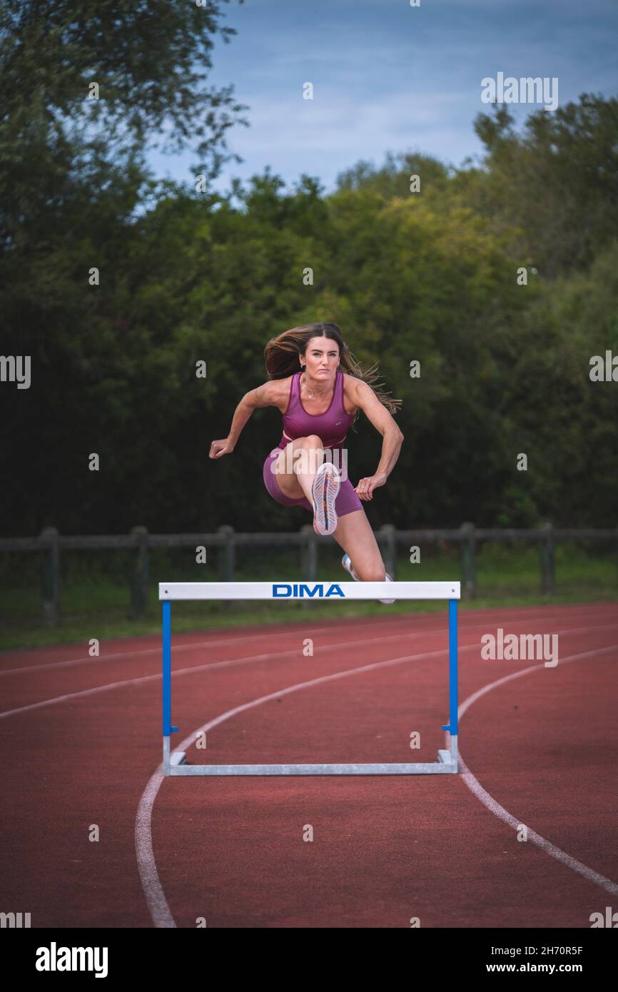 Athlete model girl jumping hurdles on the running track Stock Photo - Alamy