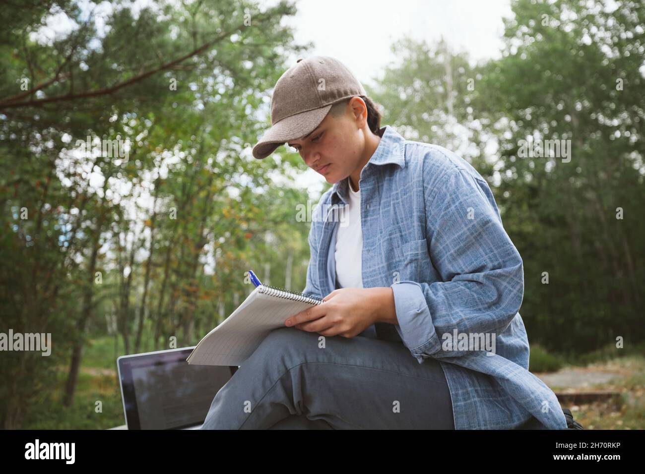 Young woman with notepad and laptop sitting on bench Stock Photo - Alamy