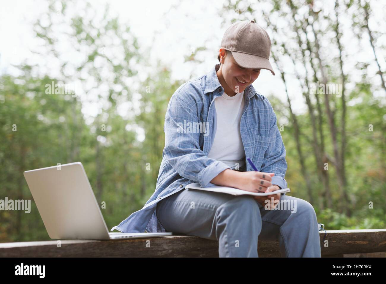 Young woman with notepad and laptop sitting on bench Stock Photo - Alamy