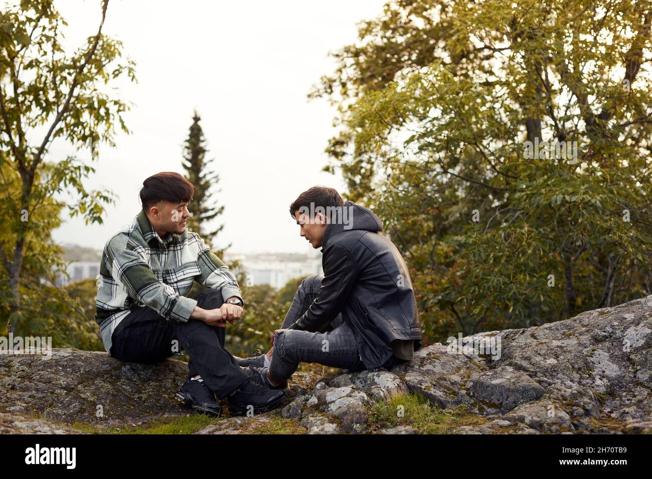 Young men sitting on rocks and talking Stock Photo - Alamy