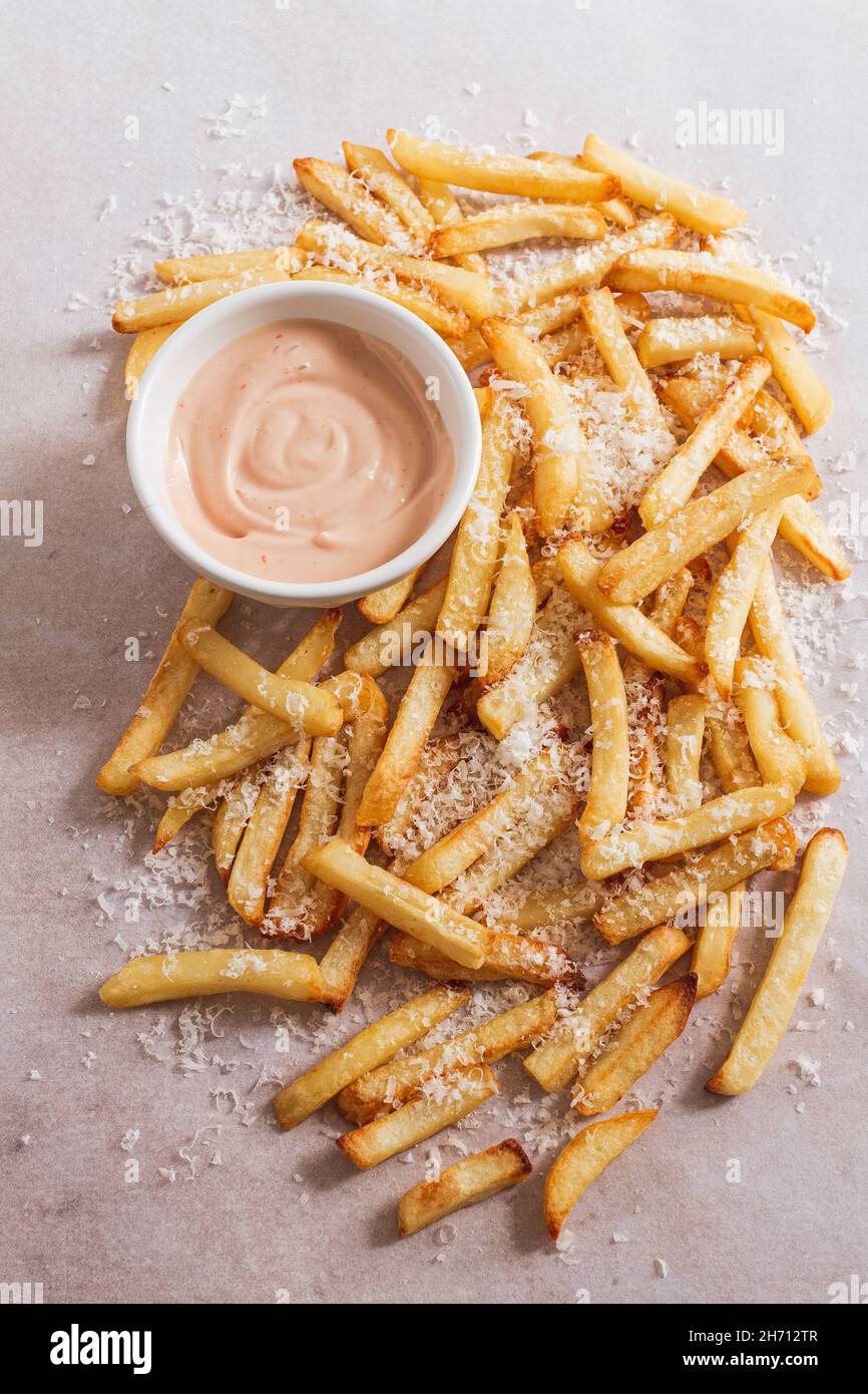 Golden French fries topped with parmesan cheese with a small bowl of ...