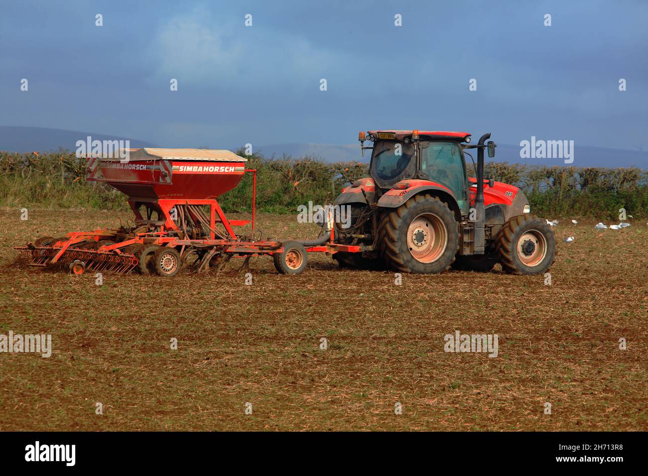 A large red Tractor running around the field sowing the seeds for ...