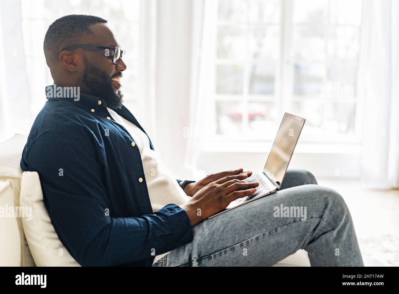 Side view at young modern African-American freelancer guy using laptop ...