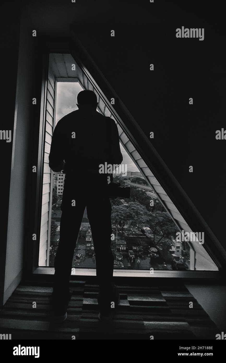 Vertical grayscale shot of a man with camera silhouette standing near ...