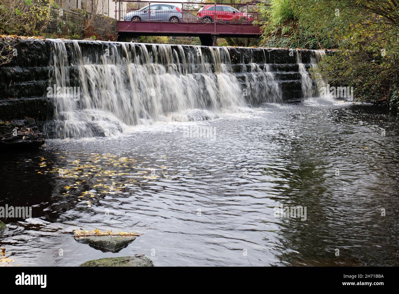 Waterfall weir flowing with metal bridge and cars in the background ...