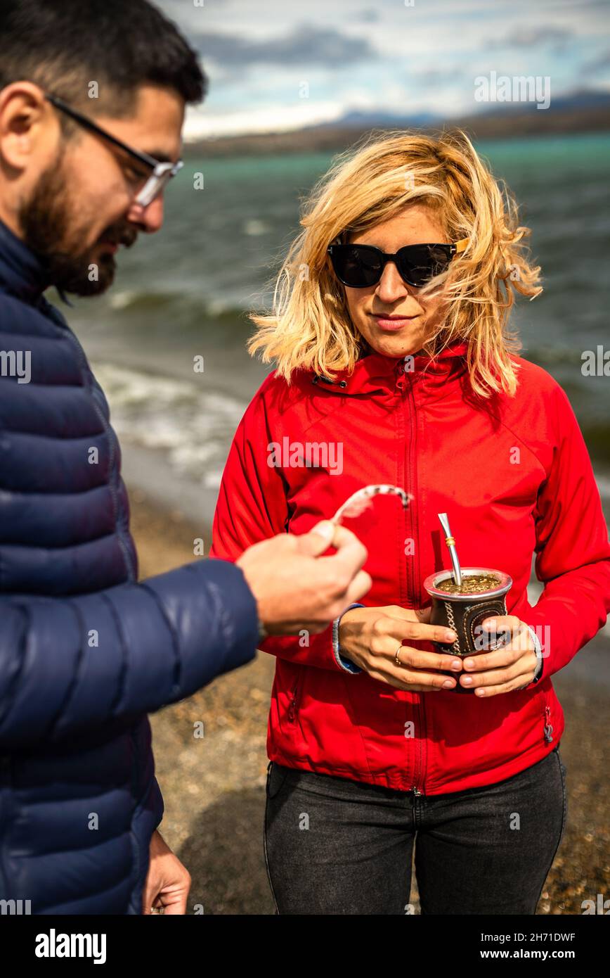 Adult Argentinian couple drinking hot mate tea at the beach on a windy ...