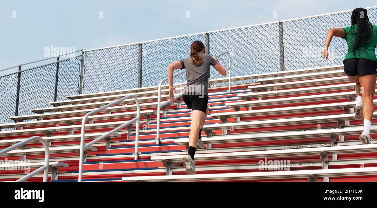 Rear view of two high school girls running up red bleachers during a ...