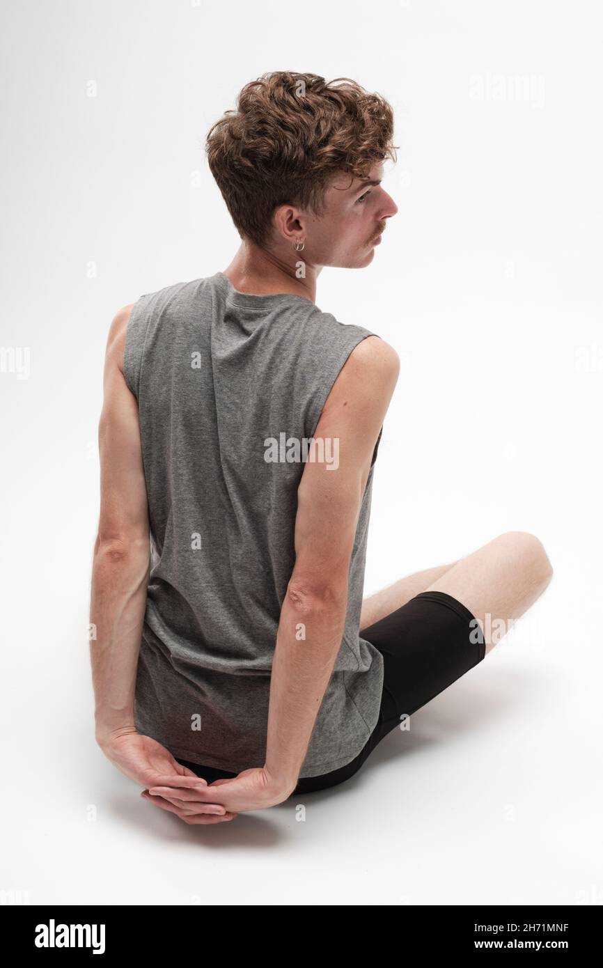 Young boy streching his arms with his legs crossed on white background ...