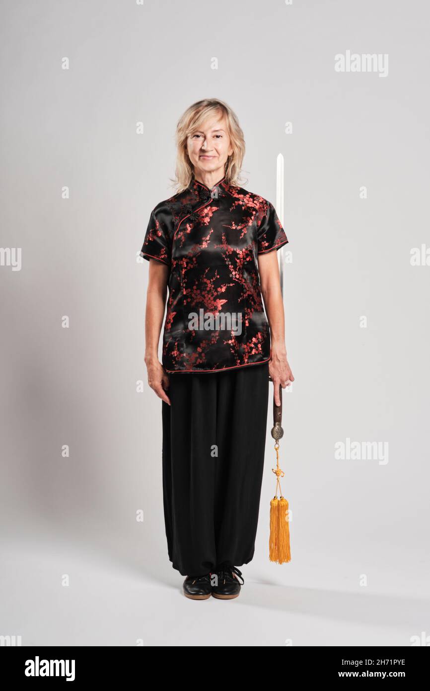 Mature blonde woman practicing Tai Chin with sword in a white ...