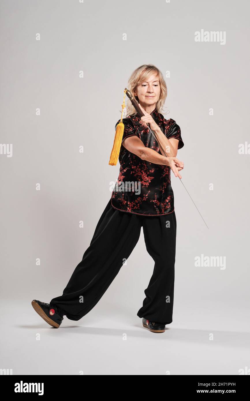 Mature blonde woman practicing Tai Chin with sword in a white ...