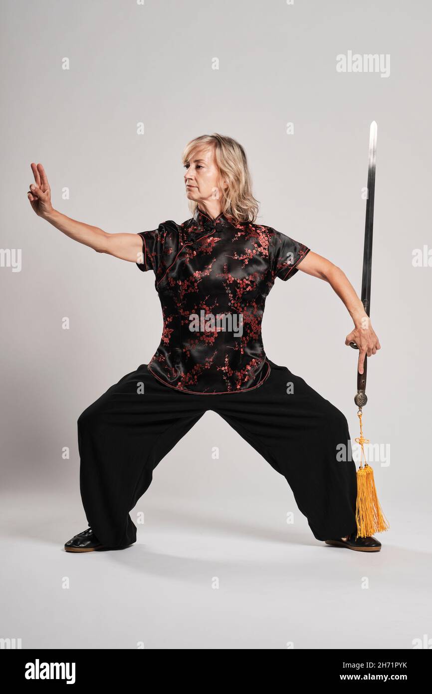 Mature blonde woman practicing Tai Chin with sword in a white ...