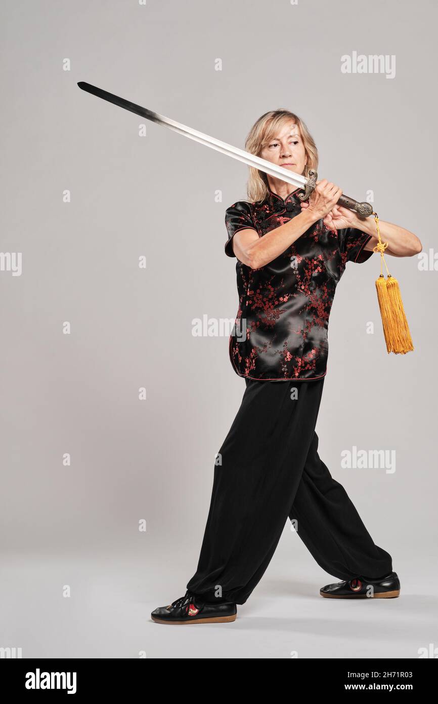 Mature blonde woman practicing Tai Chin with sword in a white ...