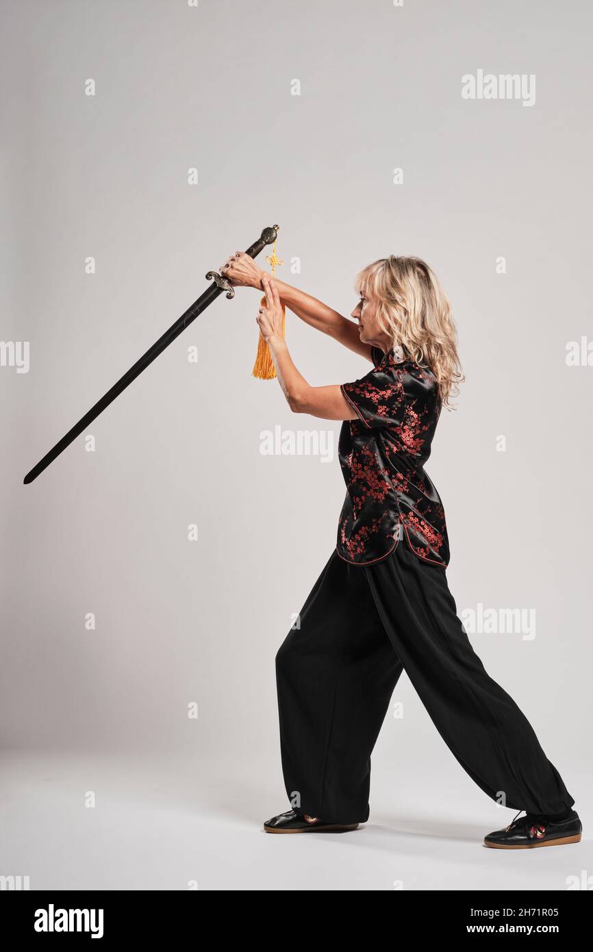 Mature blonde woman practicing Tai Chin with sword in a white ...