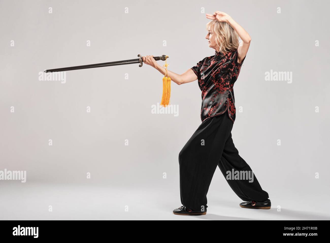 Mature blonde woman practicing Tai Chin with sword in a white ...