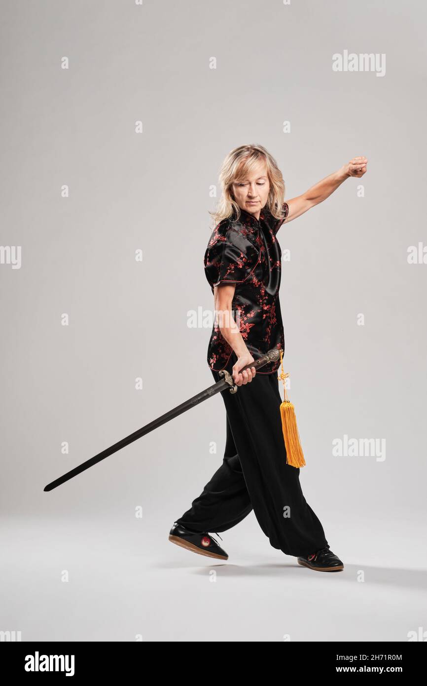 Mature blonde woman practicing Tai Chin with sword in a white ...