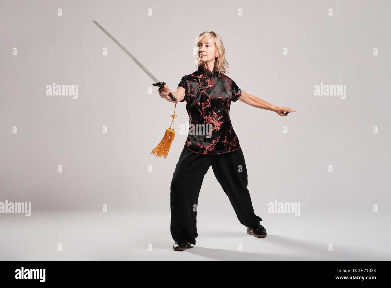 Mature blonde woman practicing Tai Chin with sword in a white ...