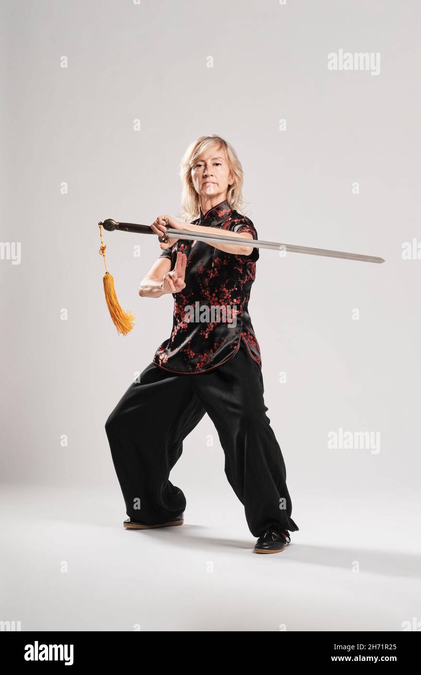 Mature blonde woman practicing Tai Chin with sword in a white ...