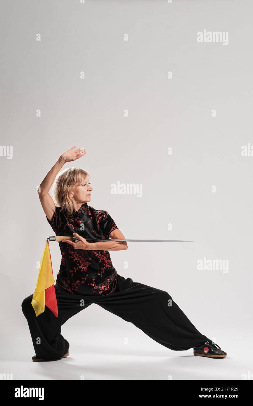 Mature blonde woman practicing Tai Chin with saber in a white ...