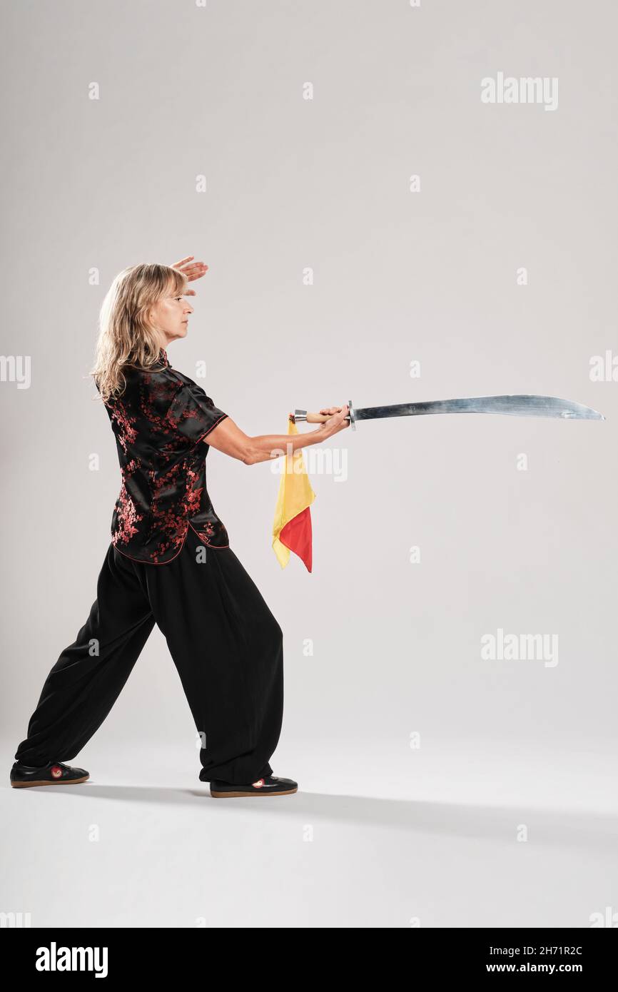 Mature blonde woman practicing Tai Chin with saber in a white ...