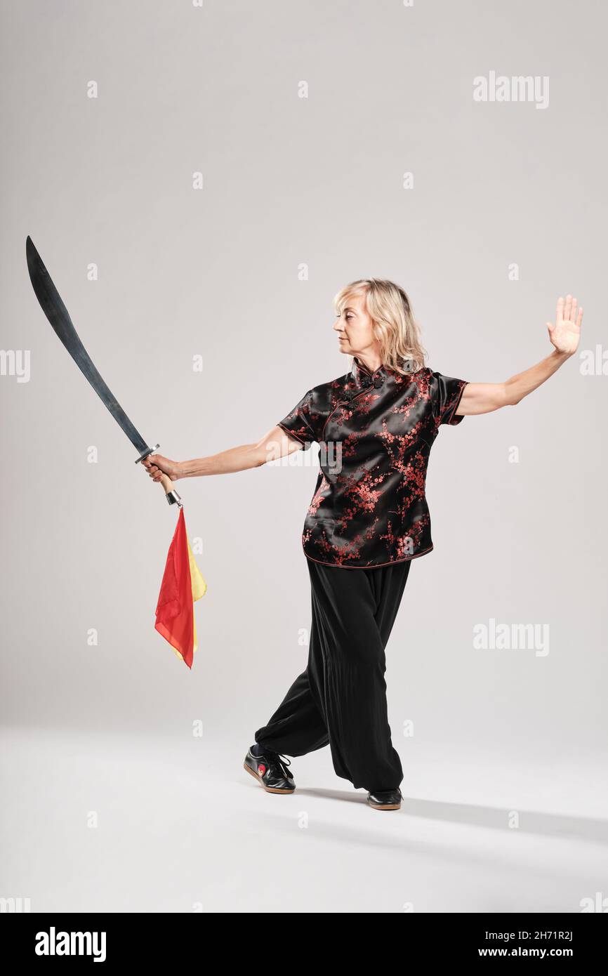 Mature blonde woman practicing Tai Chin with saber in a white ...