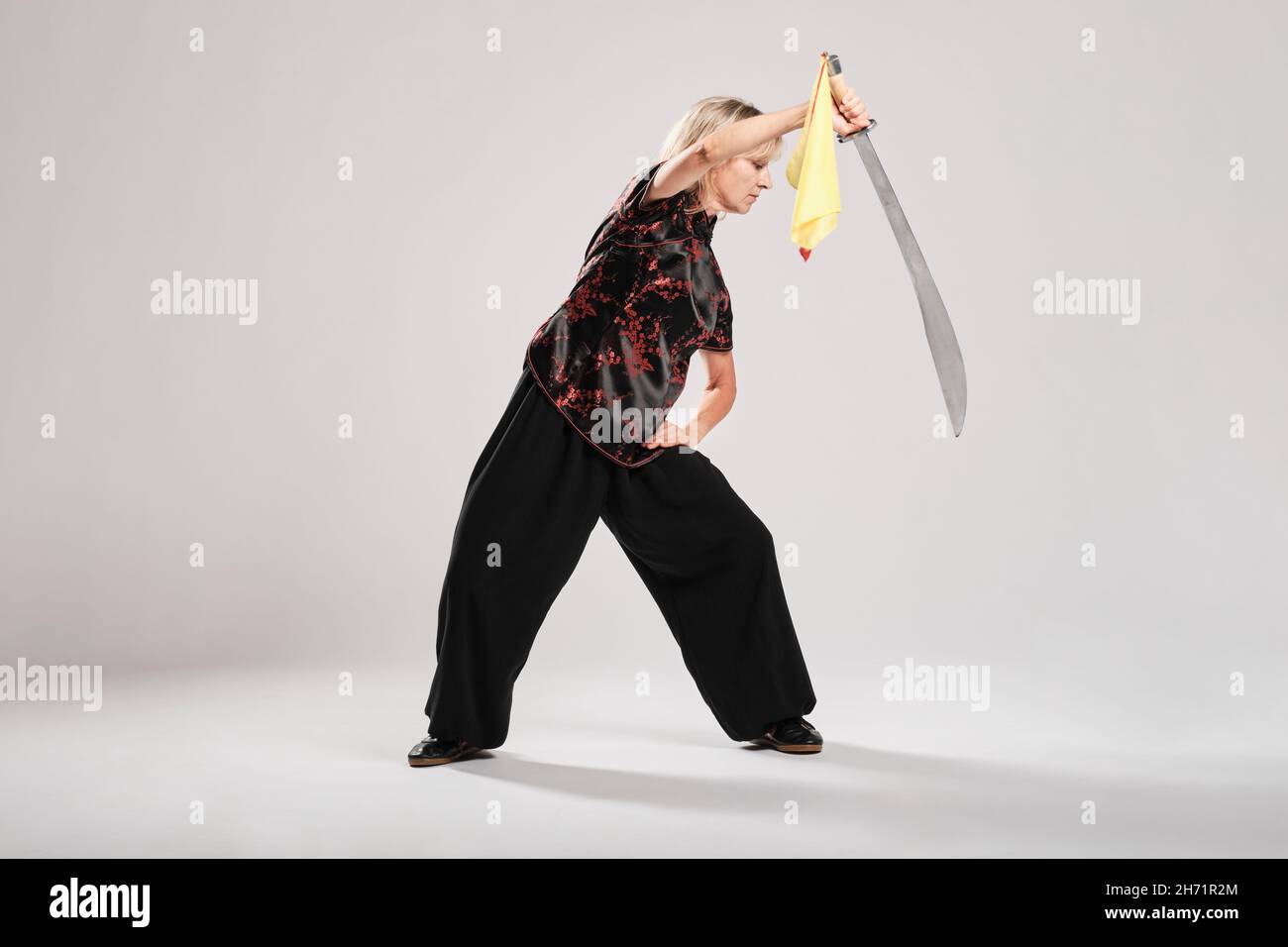 Mature blonde woman practicing Tai Chin with saber in a white ...