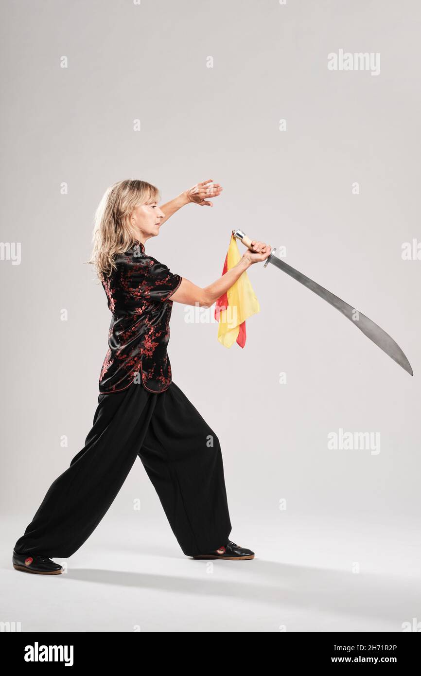 Mature blonde woman practicing Tai Chin with saber in a white ...