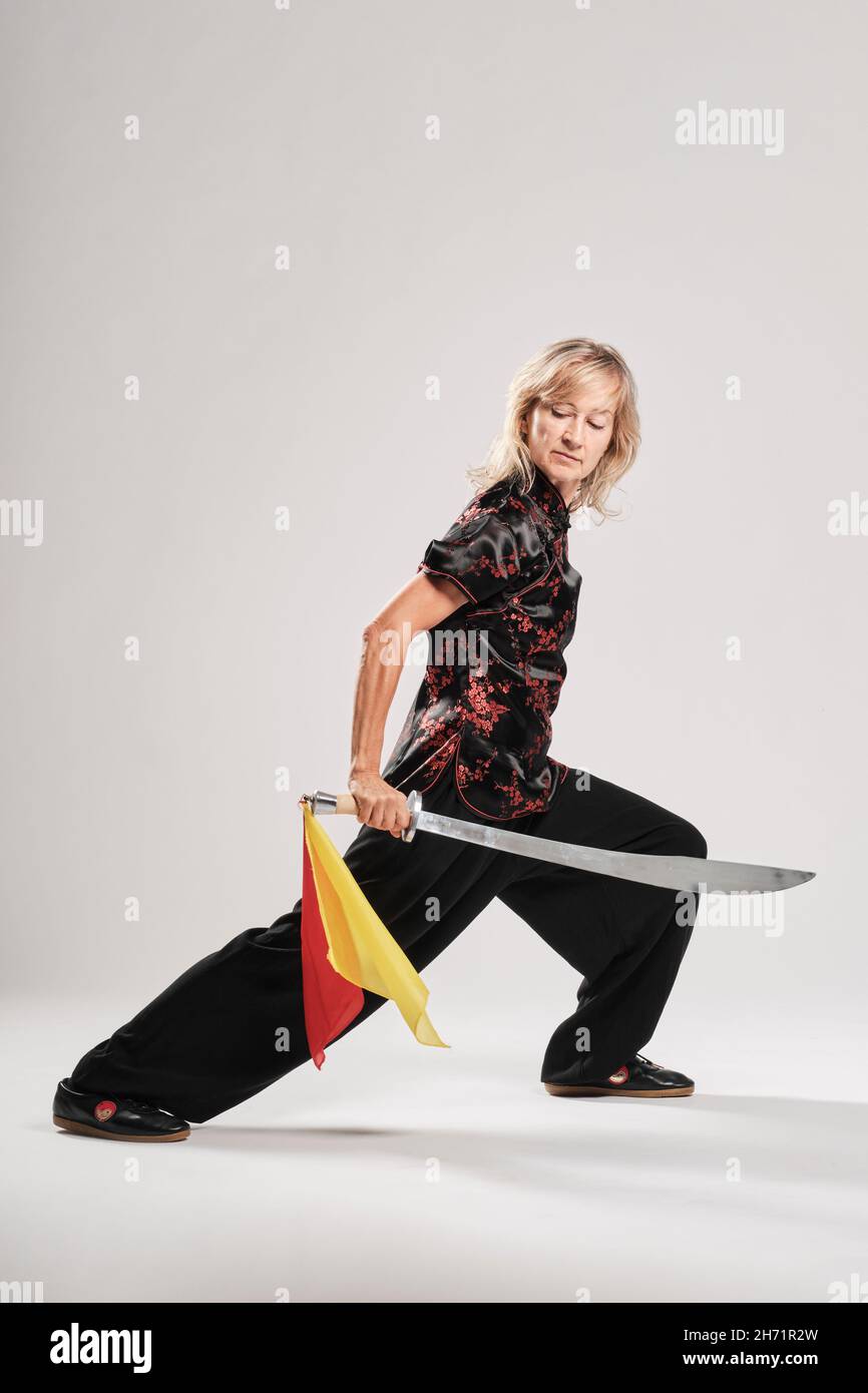 Mature blonde woman practicing Tai Chin with saber in a white ...