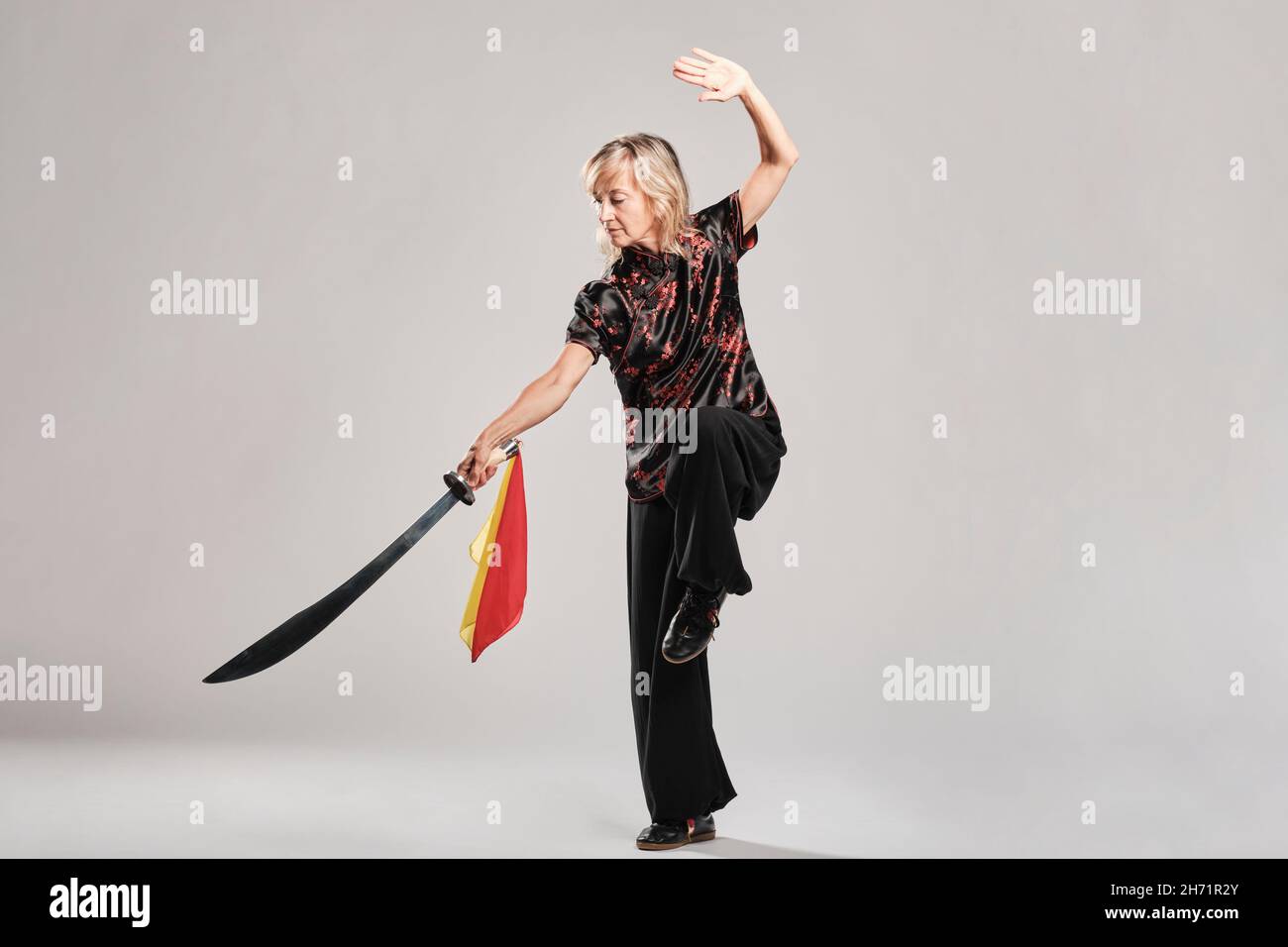 Mature blonde woman practicing Tai Chin with saber in a white ...